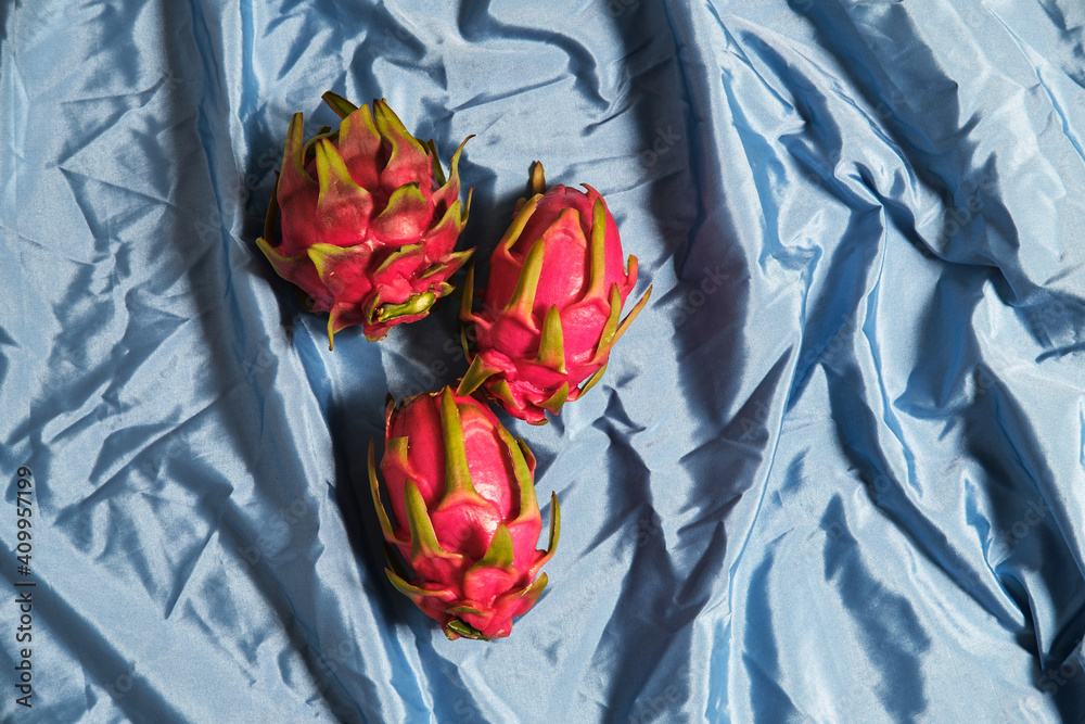 From above of whole fresh pitaya fruits arranged on blue wrinkled cloth ...