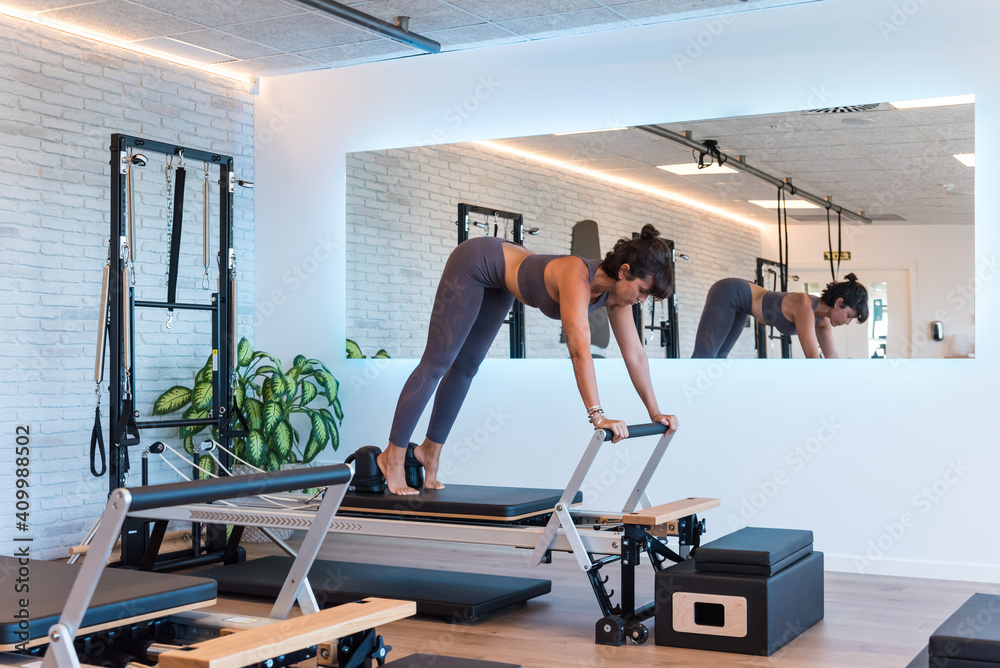 Slim adult female stretching body on modern reformer during Pilates ...