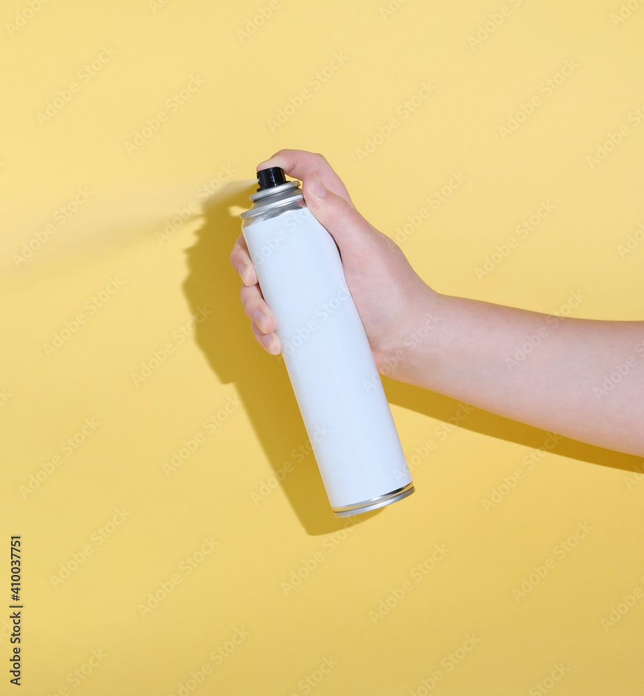 hand holding a tin can and spraying a product over a yellow background ...