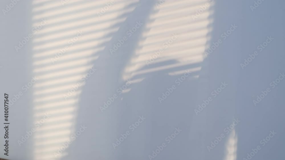 shadows on the wall from a window closed with blinds and a woman's ...