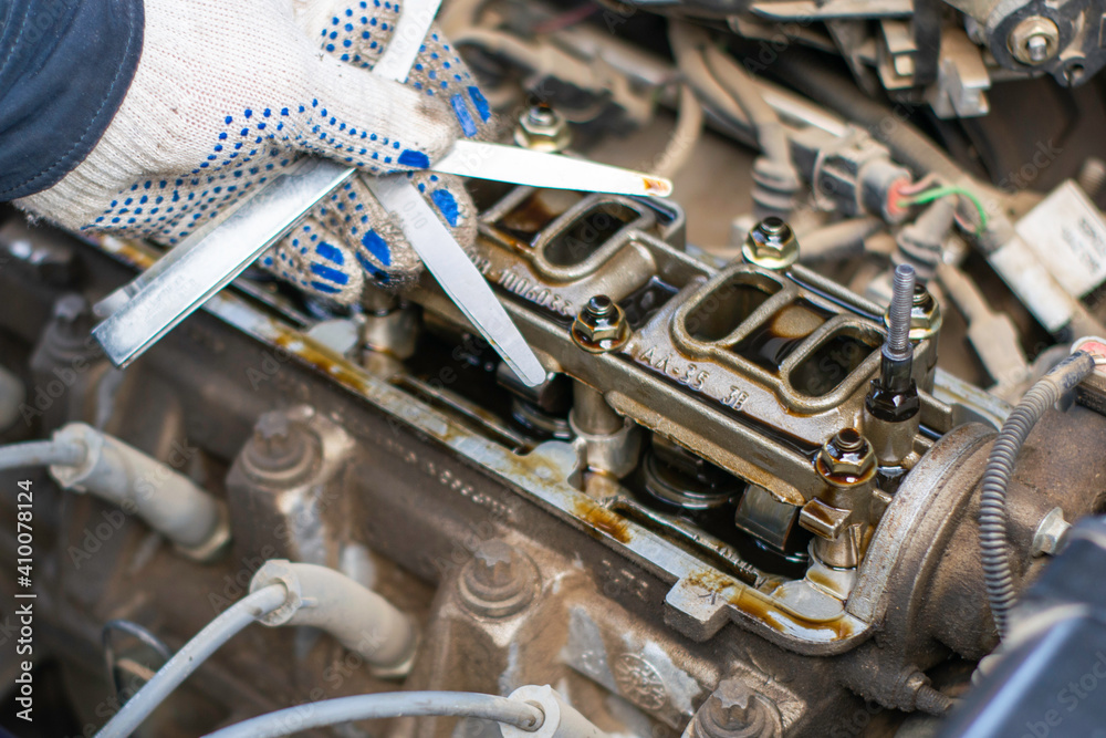 the mechanic adjusts the gap in the valve mechanism of the car engine ...