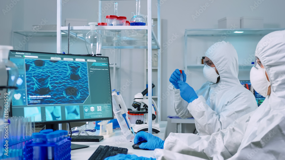 Chemist doctor in ppe suit working at pc while lab technician using ...