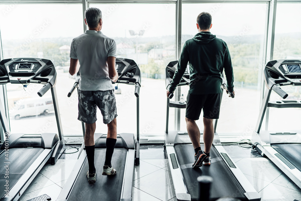 Two men on a treadmill in a modern gym, in front of them are large ...