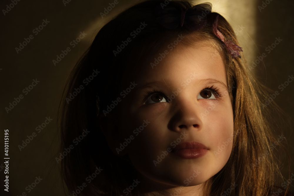 Little girl in dark side with shadow on face with blissful eyes looking ...