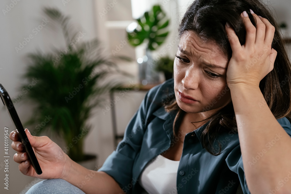 Sad woman sitting on the couch, using the phone. Upset woman waiting ...