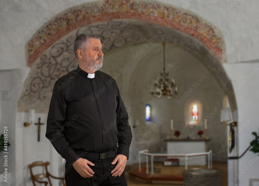 A priest in a black shirt with a white clerical collar stands in a ...