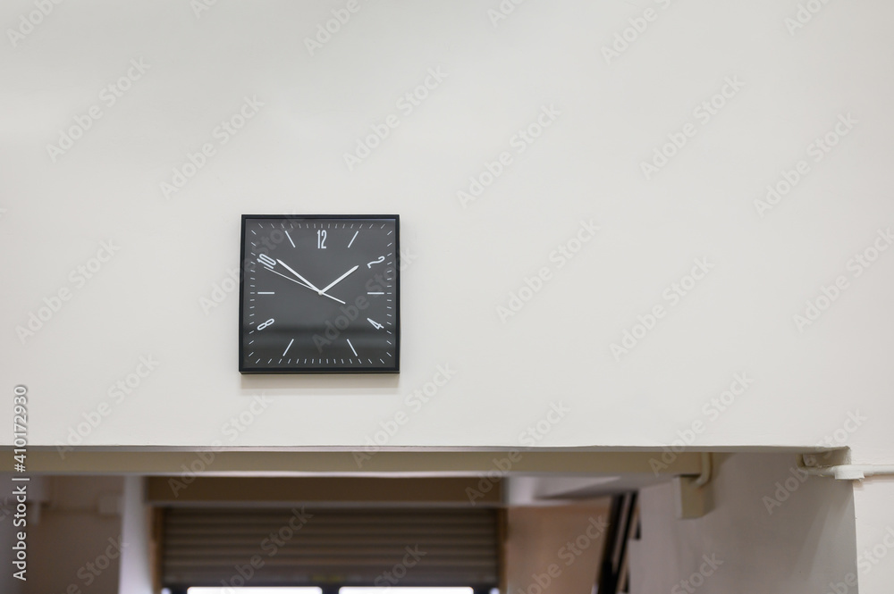 Black clock in square shape on the concrete white wall of the mezzanine ...