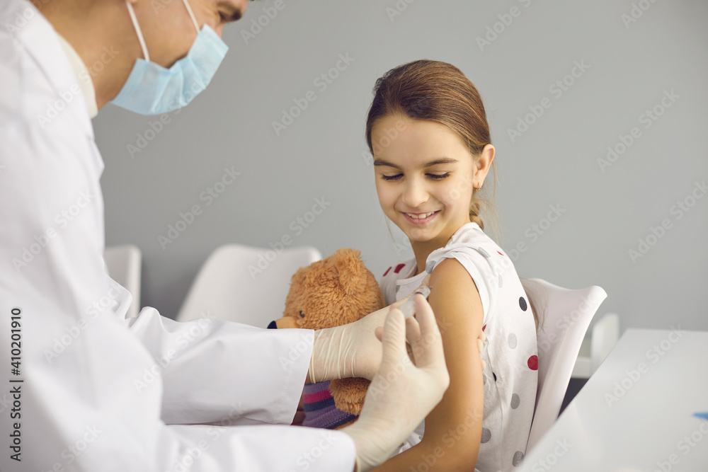 Happy little girl getting a shot at doctor's office. Male nurse giving ...