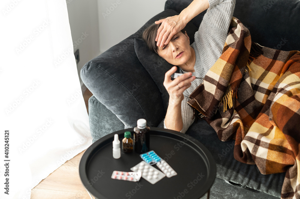Sick senior woman has fever, cold and flu symptoms, lays on the couch ...