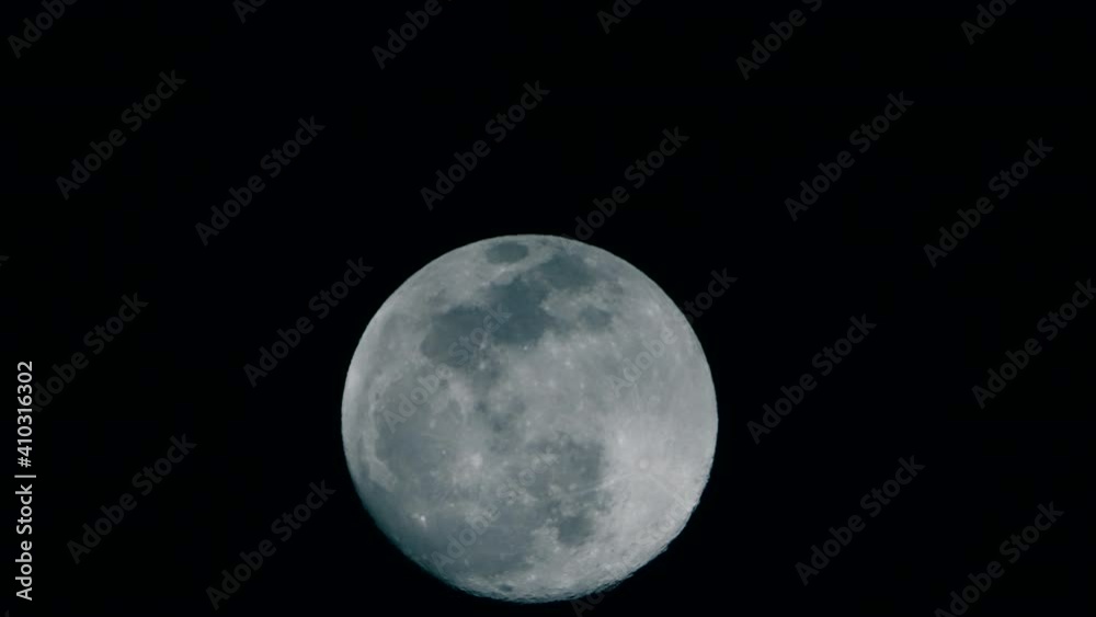 Shot of a full moon slowly rising up in the sky with thin clouds in ...