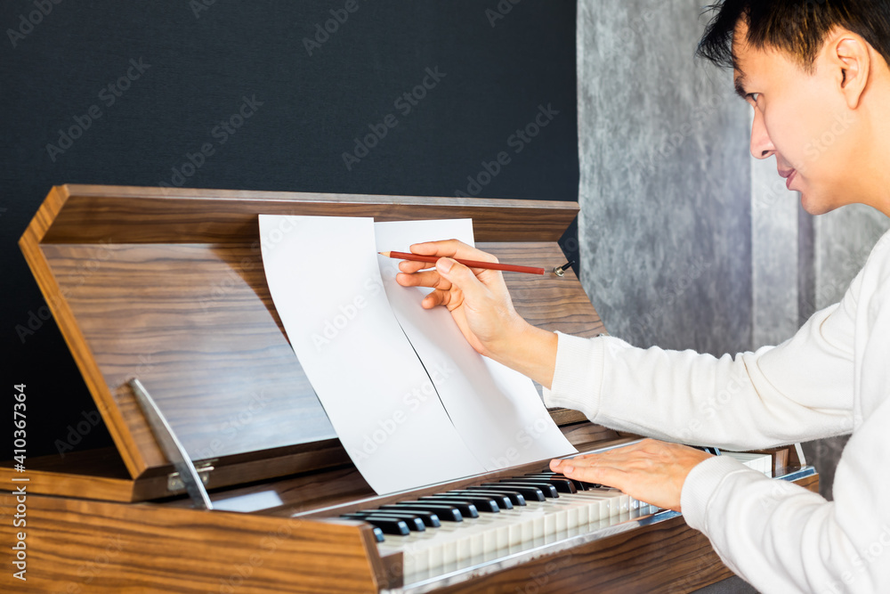 asian male songwriter writing a hit song while playing piano ...