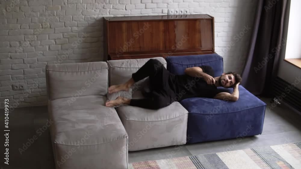 Happy man falling on the sofa, switch on the tv at home in the living ...