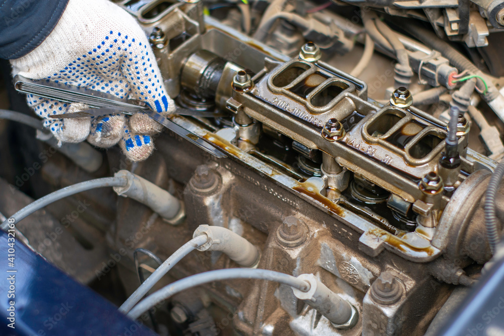 the mechanic adjusts the gap in the valve mechanism of the car engine ...