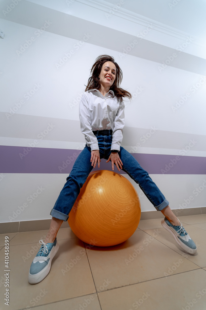 Pretty girl gumps on fitness ball. Happy and funny young woman balances ...