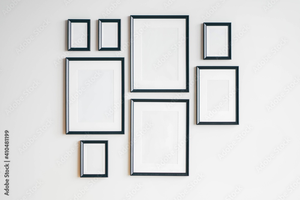Multiple many black picture frames on white wall. Woman hanging a frame ...