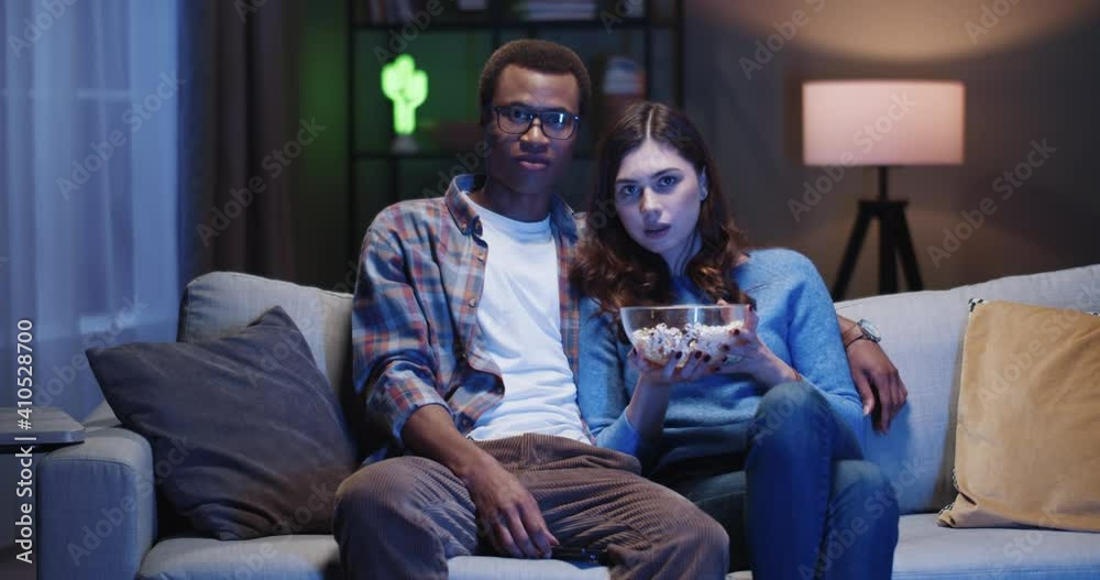 Couple sitting on sofa at home and watching scary movie at night. Two ...