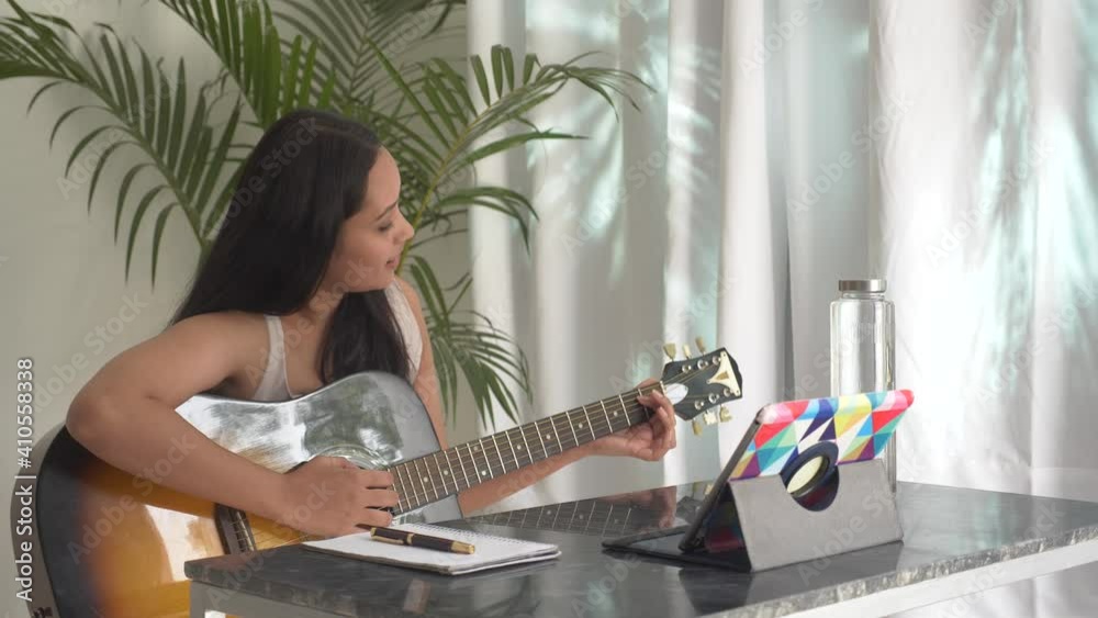 Pretty Indian girl watching online guitar lesson and practising music ...