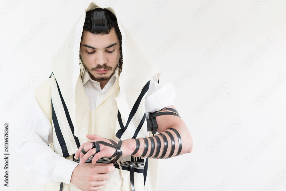 Young Orthodox Jew in shawl (tallit) putting on phylacteries (tefilin ...