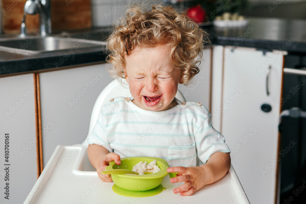 Crying Caucasian kid boy sitting in high chair with cereal puree on ...