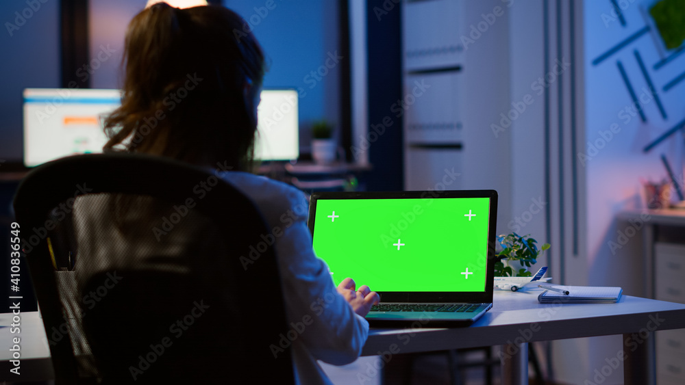 Back view of business woman looking at green screen laptop sitting at ...