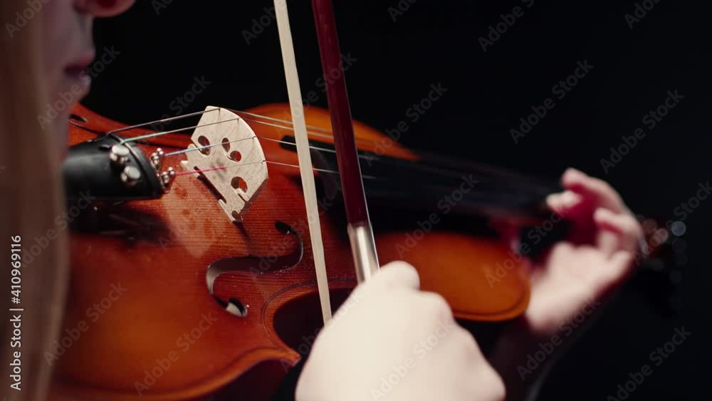 A woman musician plays a brown violin and runs a bow along the strings ...