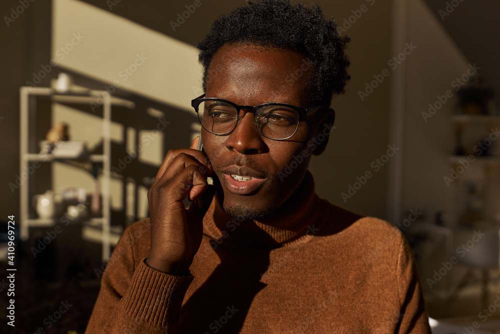 Indoor image of attractive young dark skinned man speaking on mobile ...