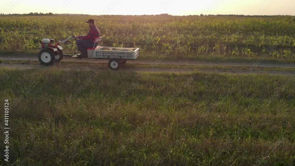 Farmer on mini tractor with trailer moves along narrow country road ...