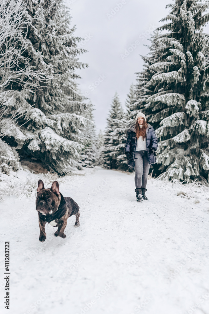 Front view of a girl walking her dog in the park through a snow-covered ...