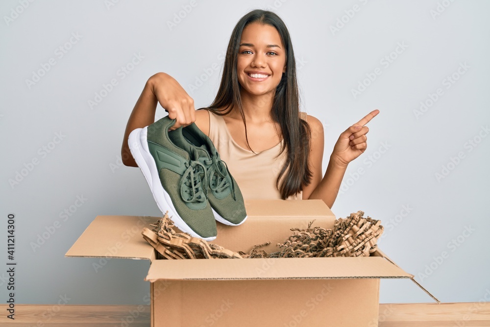 Beautiful hispanic woman taking sneaker shoes from box smiling happy ...