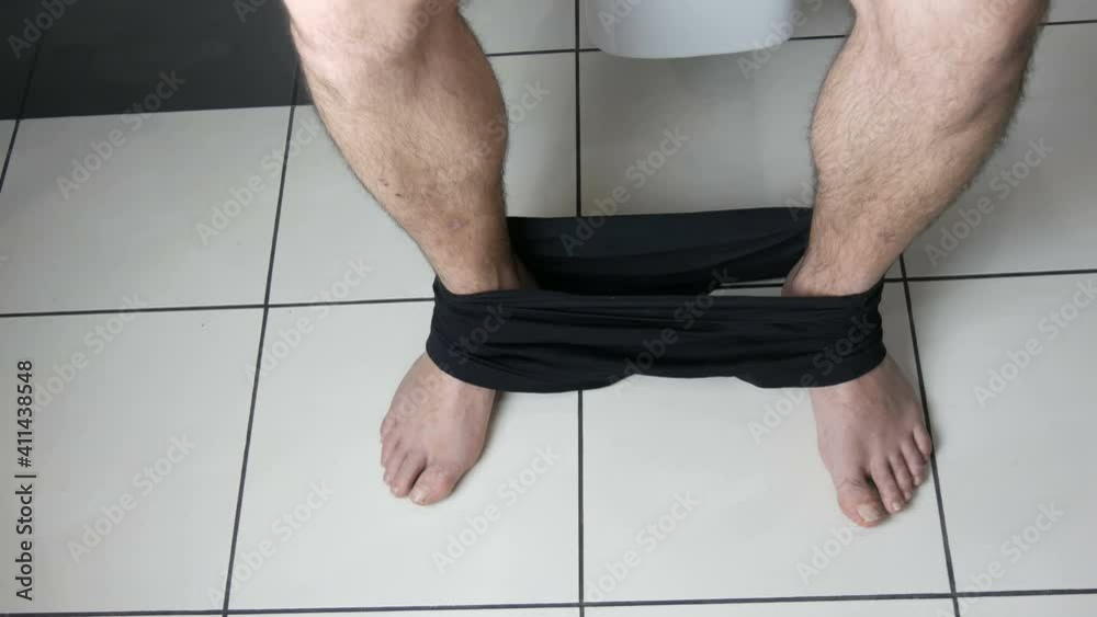 Legs of a man sitting on the toilet in the bathroom. Defecation process ...