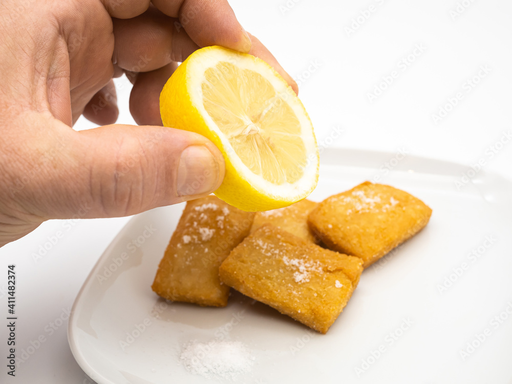 Hand squeezing a lemon on fresh panelle. Traditional Sicilian panelle ...