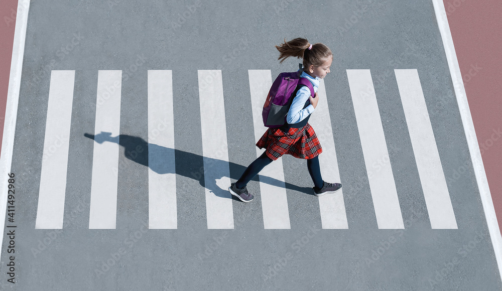 Schoolgirl crossing road on way to school. Zebra traffic walk way in ...
