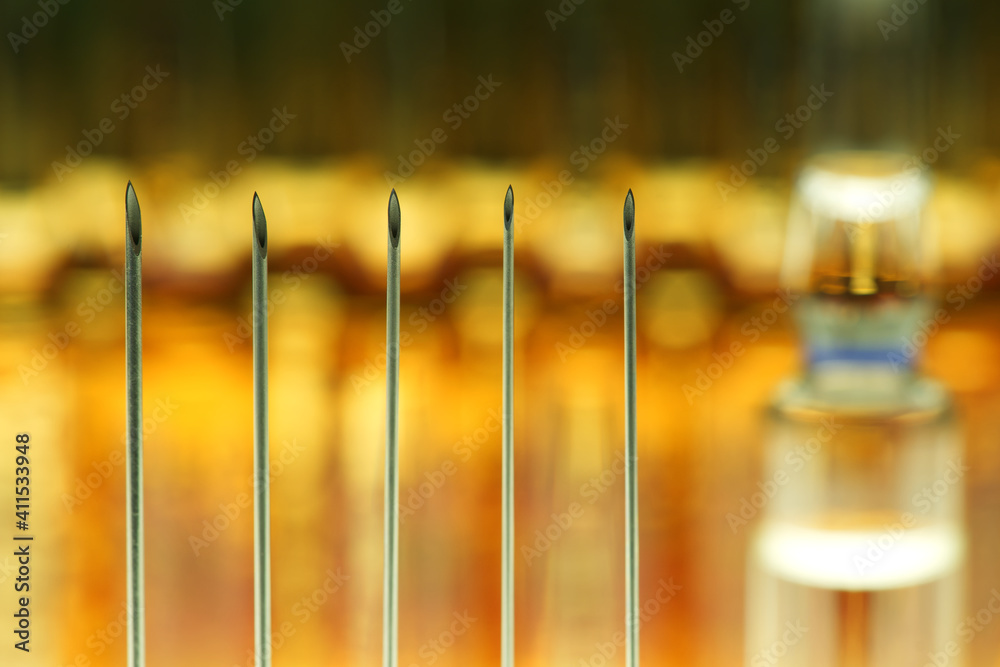 Poster Tips of disposable needles for injection, blurred brown ampules ...
