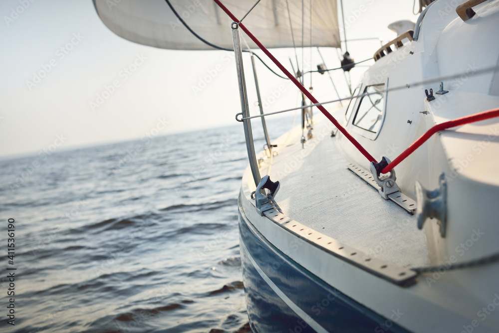 White sloop rigged yacht sailing in an open sea at sunset. Clear sky. A ...