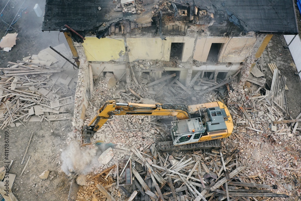 Yellow excavator destroys building. Heavy duty machine is demolishing a ...