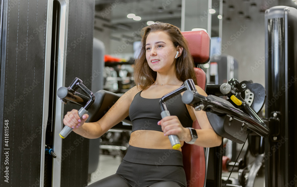 Young fit woman trains pectoral muscles in exercise machine at the gym ...