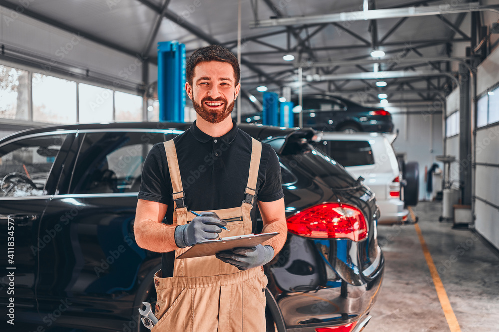 Mechanics at the repair shop. Cheerful young mechanic writing something ...