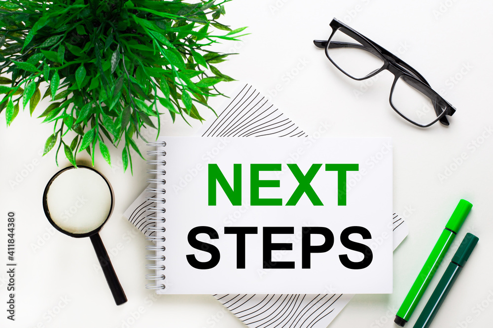 On a white background lies a notebook with the word NEXT STEPS, glasses ...