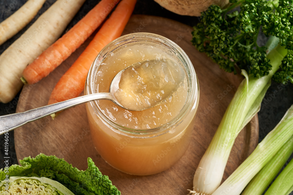Cooled congealed beef bone broth on a spoon above a glass jar Stock ...