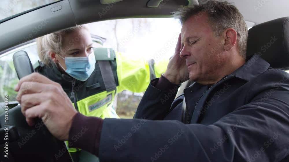 Female paramedic medic wearing face mask assessing injuries to mature ...