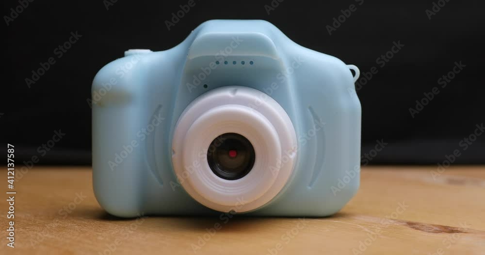 Tiny plastic photo camera in hands put on a wooden table on a black ...