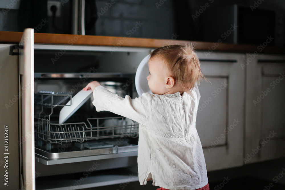 child toddler unloads the dishwasher on his own in a Scandinavian-style ...