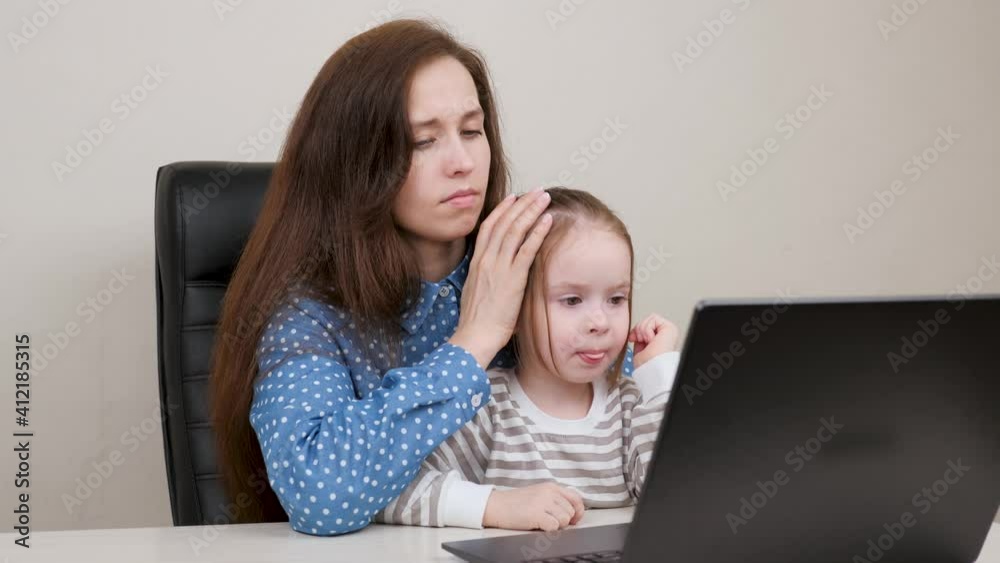 Mother works with a laptop and plays with her little daughter. Mom and ...