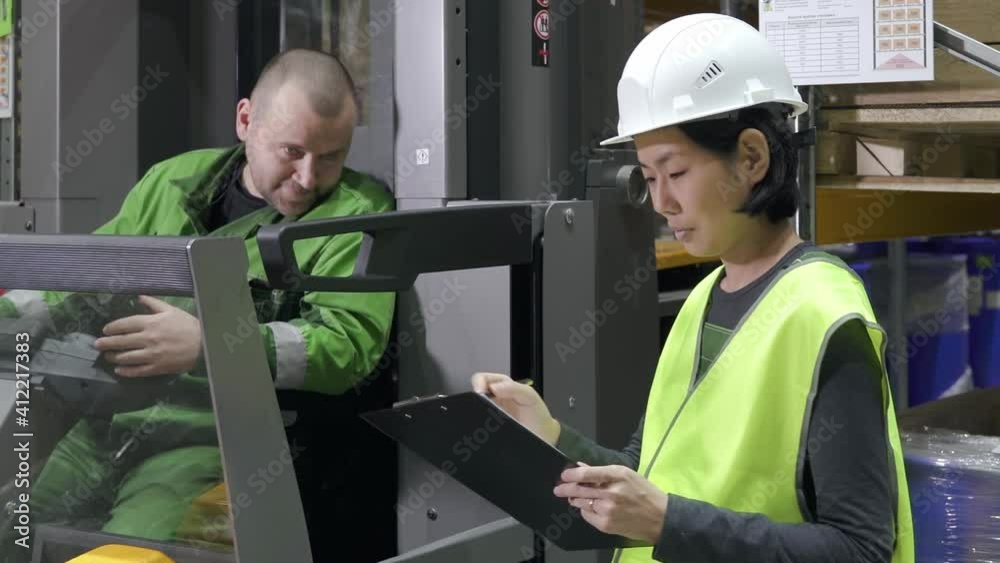 Manual worker on forklift loader and manager with clipboard at ...