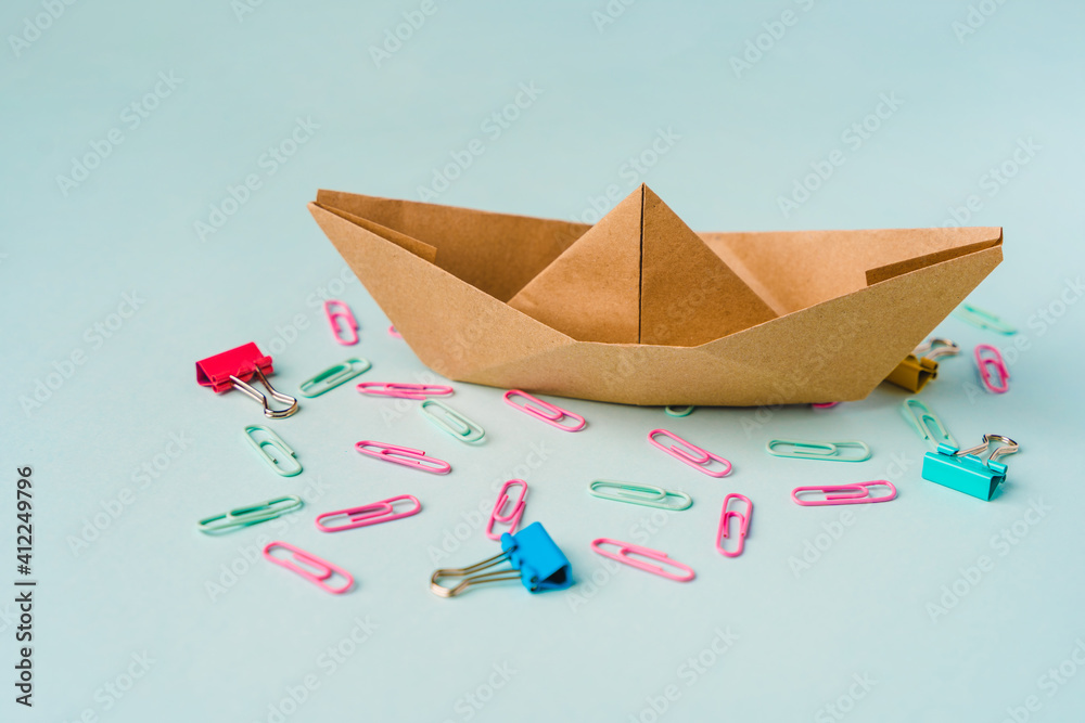 Paper boat made of craft paper on a light blue background surrounded by ...
