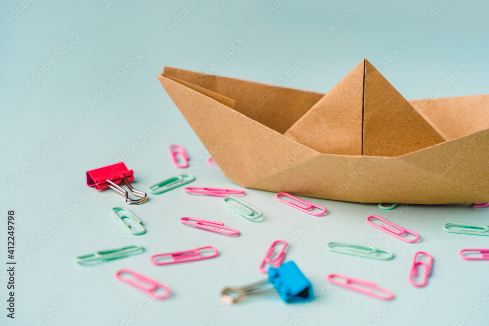 Paper boat made of craft paper on a light blue background surrounded by ...