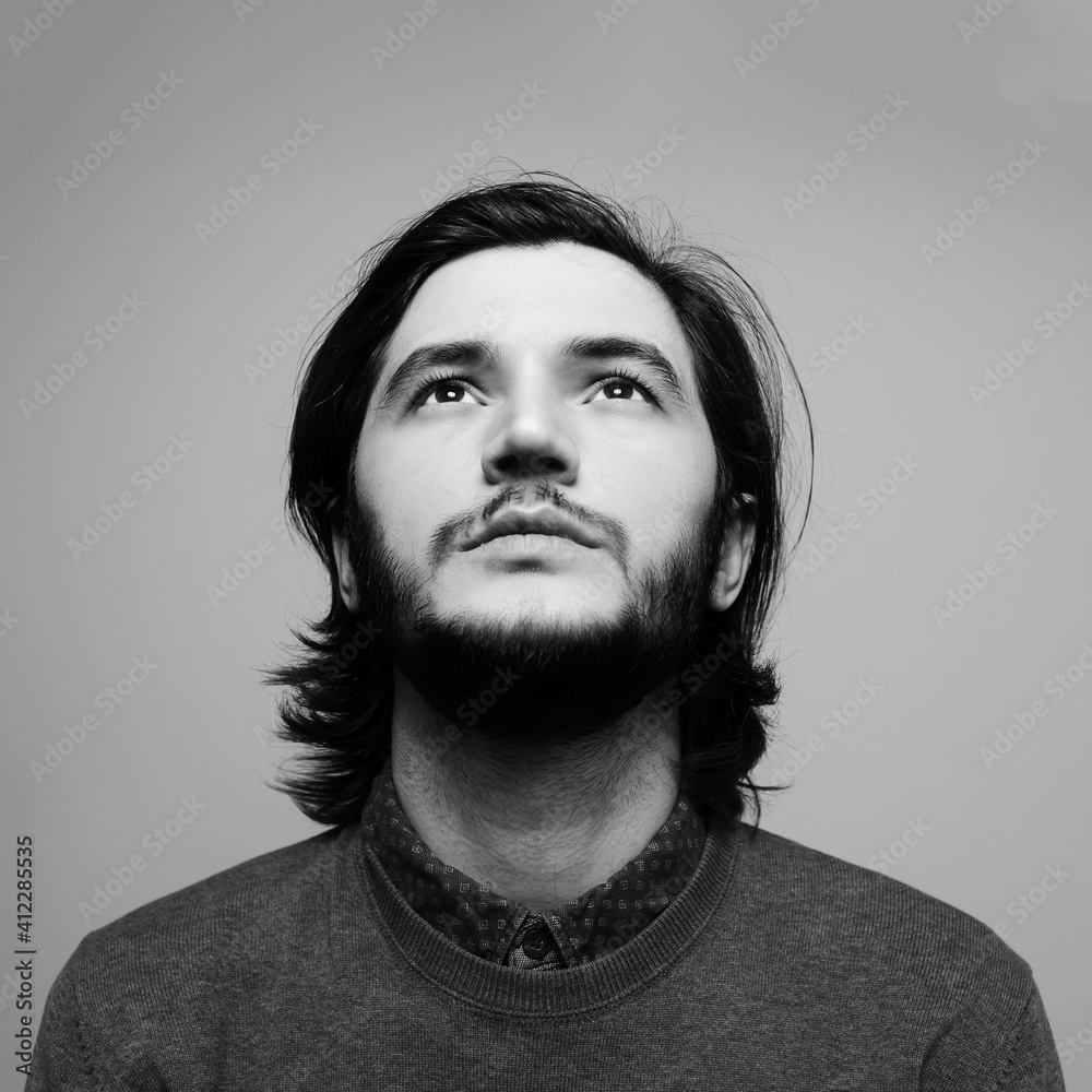 Black and white portrait of young guy with long hair looking up on grey ...