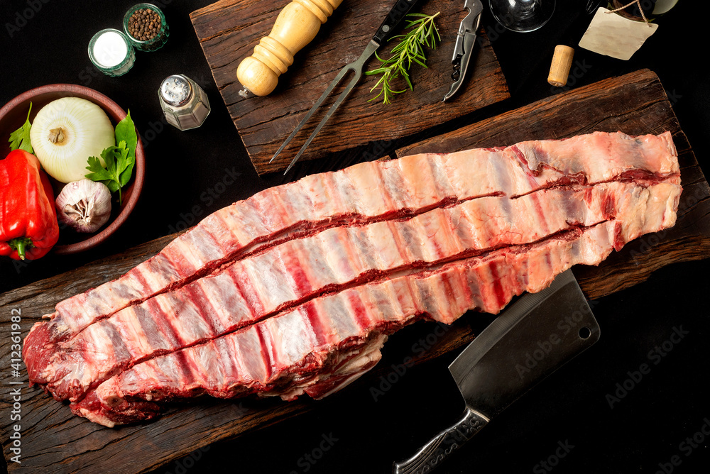 strip of roast beef, fresh beef ribs, on wooden board with vegetables ...
