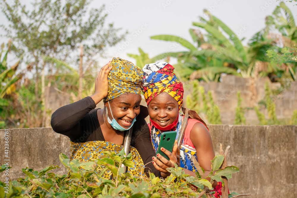Two beautiful African female farmers with nose mask, looking happily ...