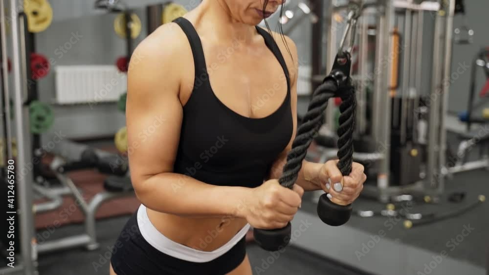 Beautiful woman works out in the gym. She pulls the rope in a crossover ...